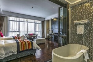 Quarto de hotel com duas camas, uma banheira grande, uma escrivaninha e vista para a cidade.