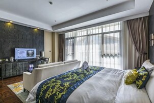 Quarto de hotel com cama grande, escrivaninha, televisão e vista para o exterior.