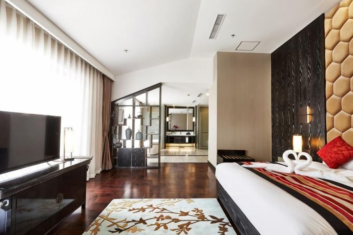 Quarto de hotel com uma cama grande, televisão, escrivaninha e vista para o banheiro.