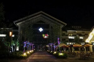 Um edifício com entrada central, rodeado por mesas ao ar livre e luzes decorativas.