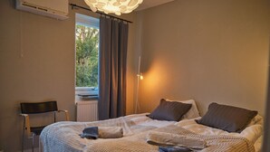 Quarto com cama grande, uma cadeira, radiador e janela com cortinas.