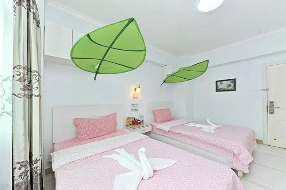 Quarto de hotel com duas camas, cada uma com roupa de cama rosa e toalhas brancas. Há decorações em formato de folha verde no teto.