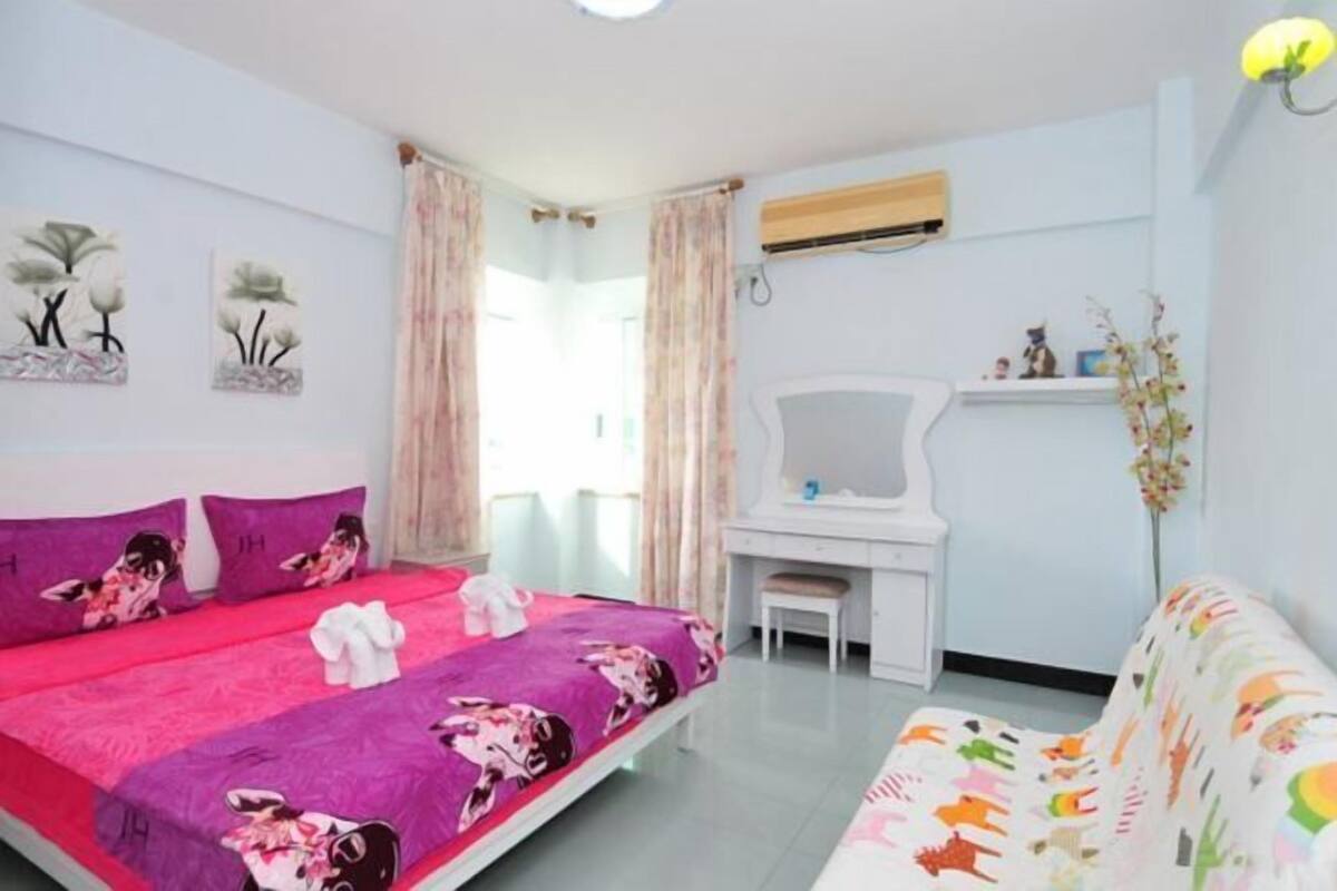 Quarto com cama, escrivaninha, poltrona, sofá e ar condicionado fixado na parede.