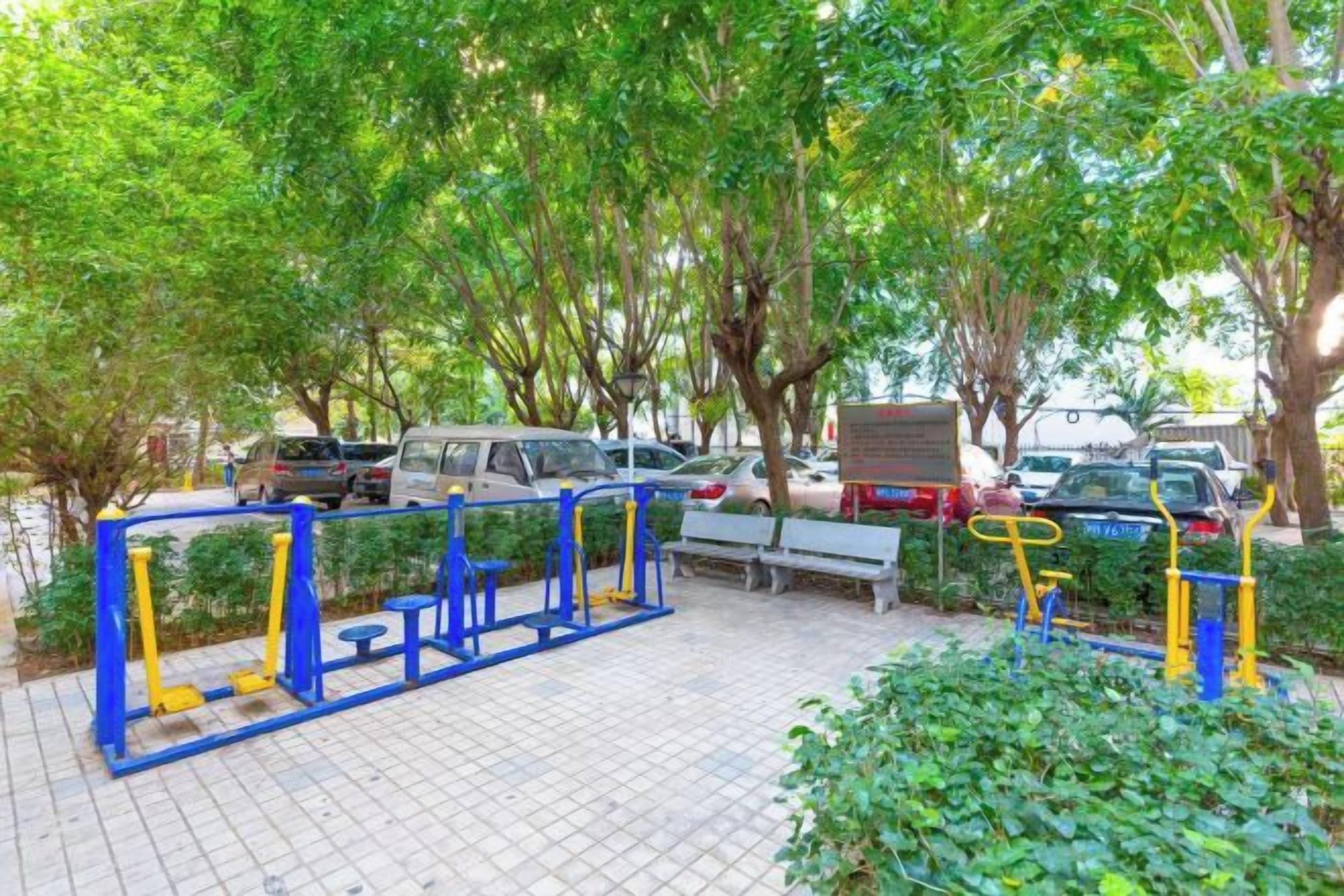 Espaço de exercícios ao ar livre com equipamentos de ginástica, um banco e carros estacionados.