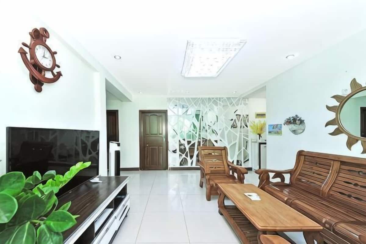 Uma sala de estar com televisão, móveis de madeira, um relógio e um painel decorativo na parede.