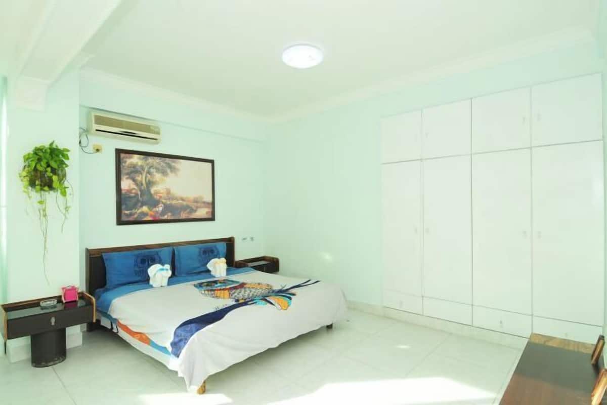 Um quarto com uma cama, mesa de cabeceira, ar-condicionado fixado na parede, um quadro e um guarda-roupa.