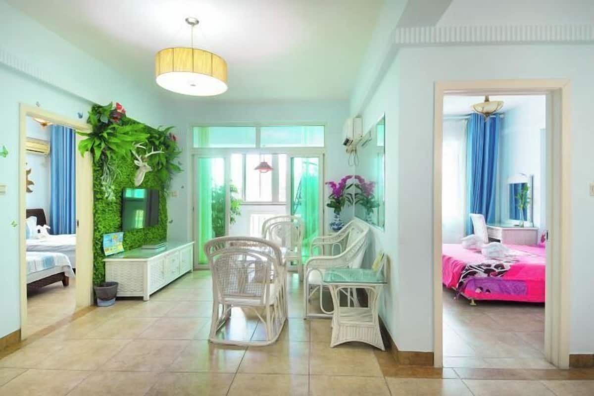 Quarto espaçoso com cama, escrivaninha e cadeira. Há uma janela com cortinas, uma parede coberta de plantas e uma luminária no teto.