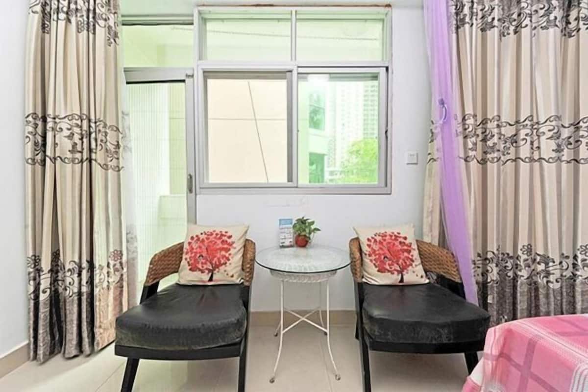 Quarto com duas cadeiras, uma mesa pequena, janela e cortinas.