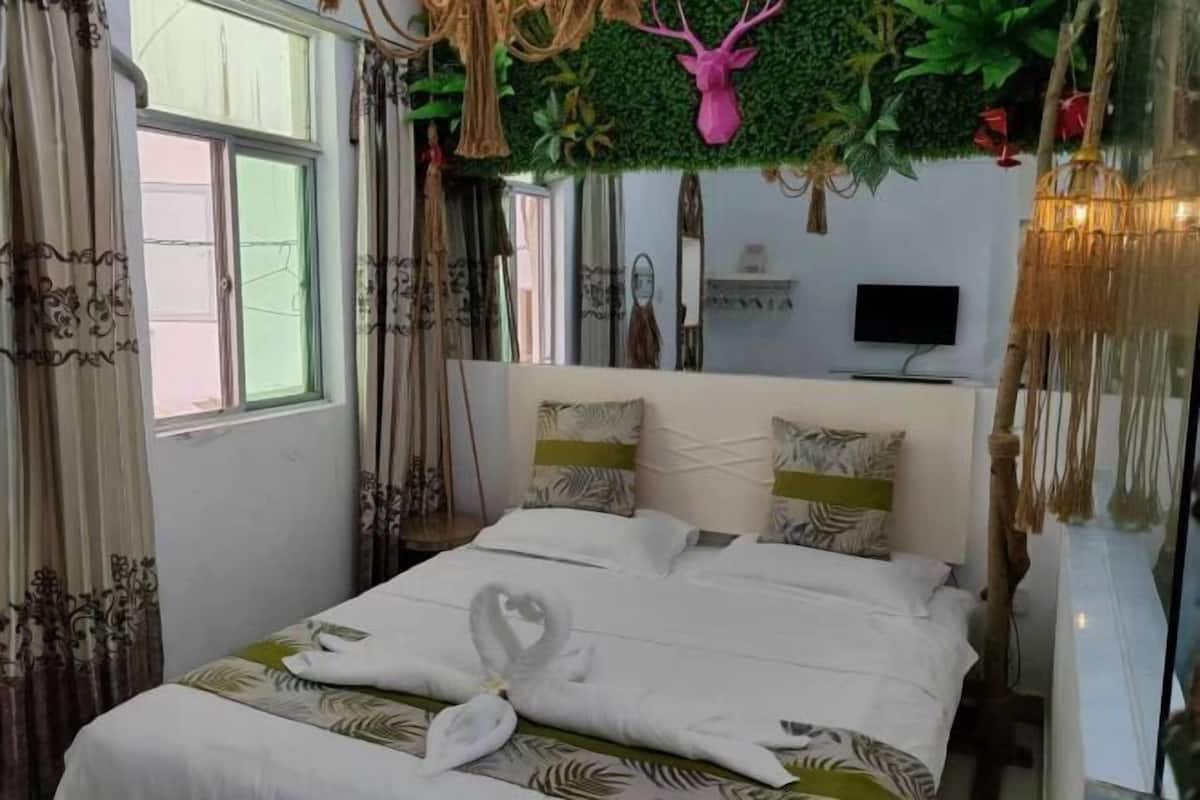 Uma cama bem arrumada com uma toalha em formato de coração, uma televisão na parede e uma decoração de parede com cabeça de veado.
