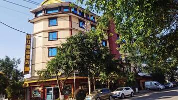 Hotel de vários andares com entrada imponente, restaurante visível e carros estacionados.