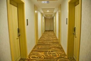 Corredor de hotel com piso carpeteado, portas de madeira e luminária no teto.