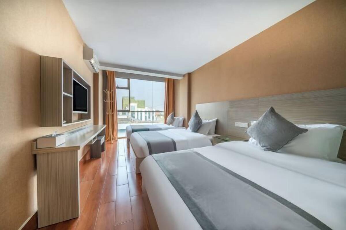 Quarto de hotel com duas camas, uma escrivaninha, televisão e uma grande janela com vista.
