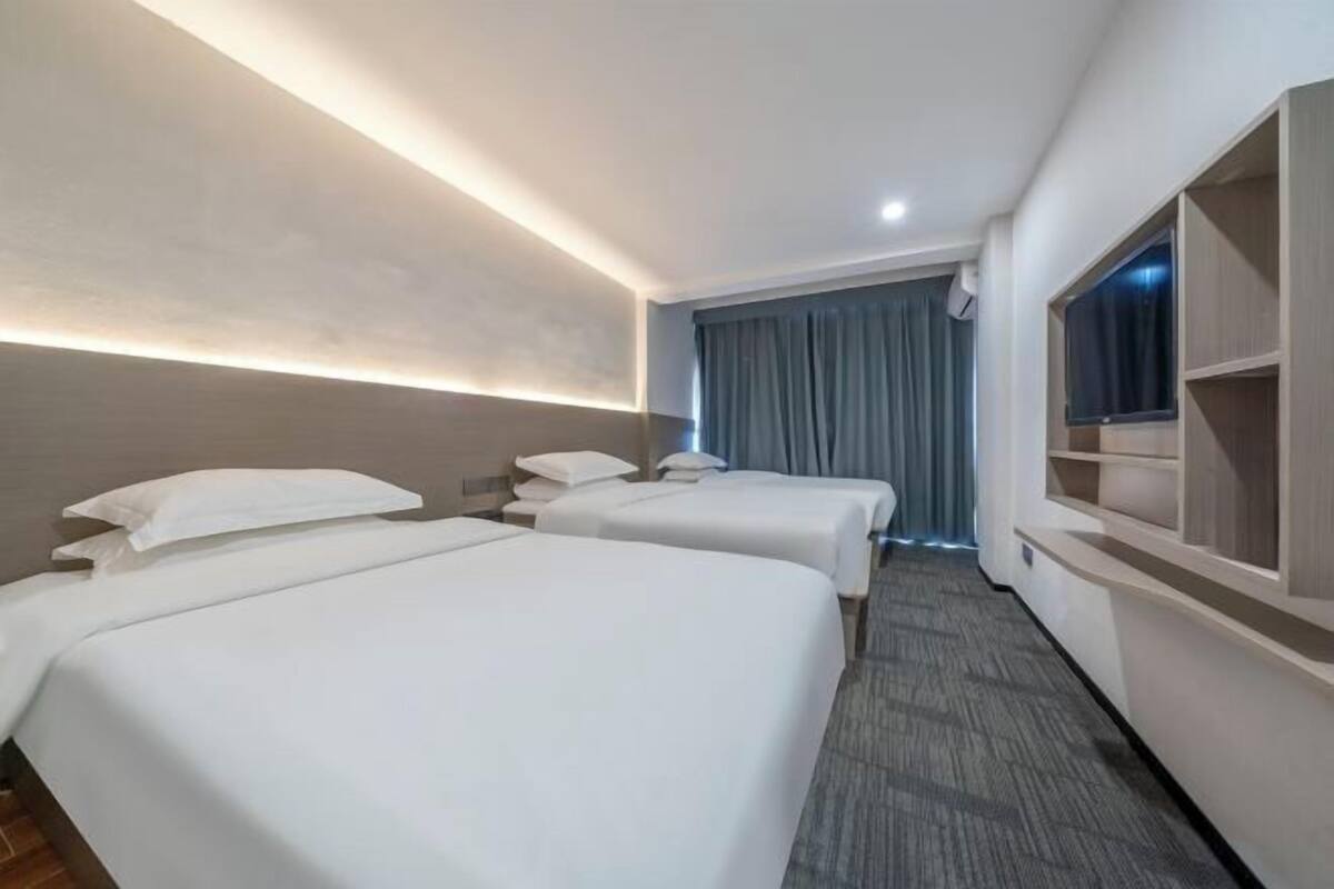 Quarto de hotel com duas camas, televisão e uma janela grande com cortinas.