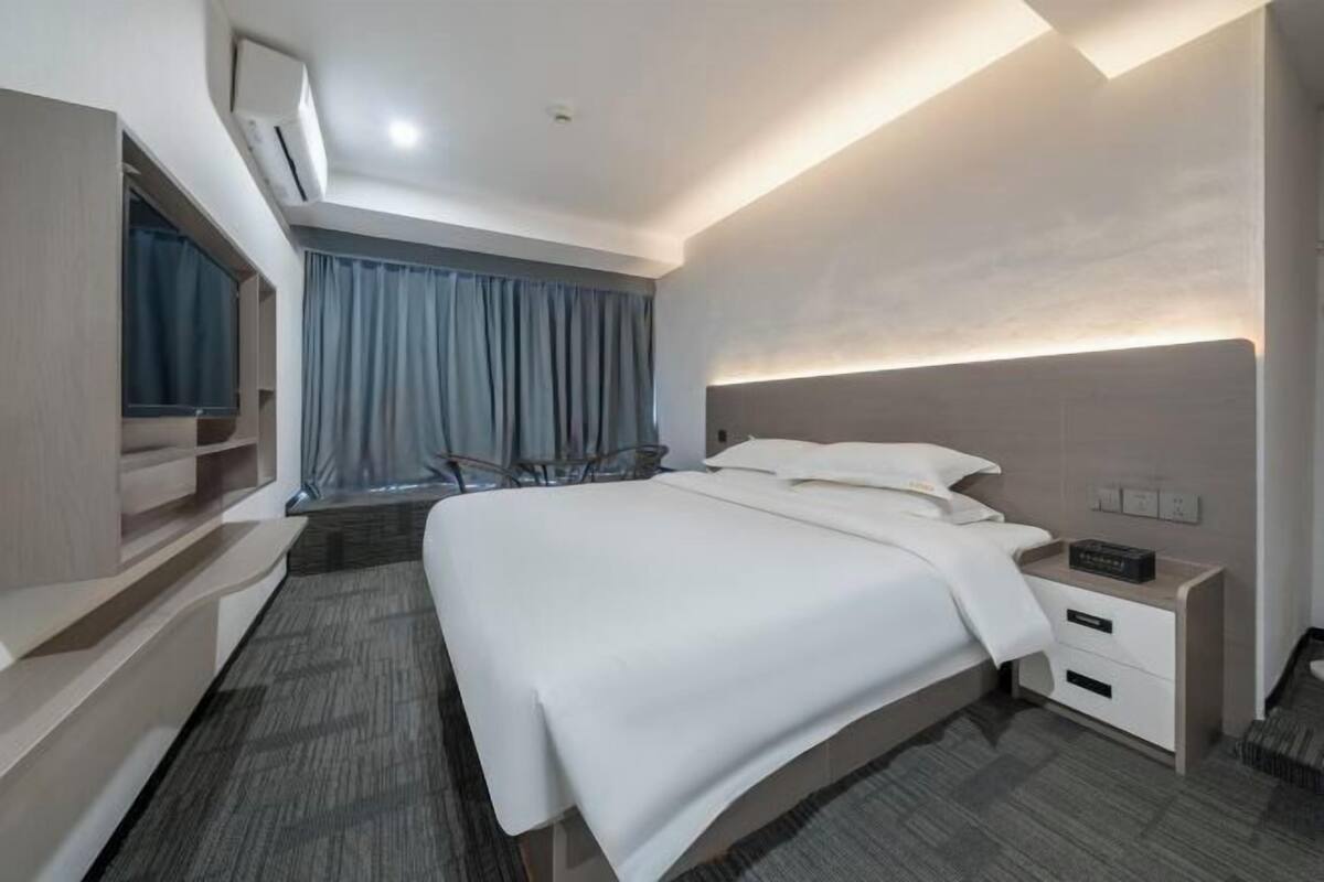Quarto de hotel moderno com uma cama grande, televisão, secretária e uma cadeira.