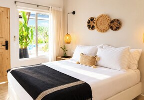 Quarto com cama, janela com cortinas, mesa de cabeceira com abajur e decoração na parede.