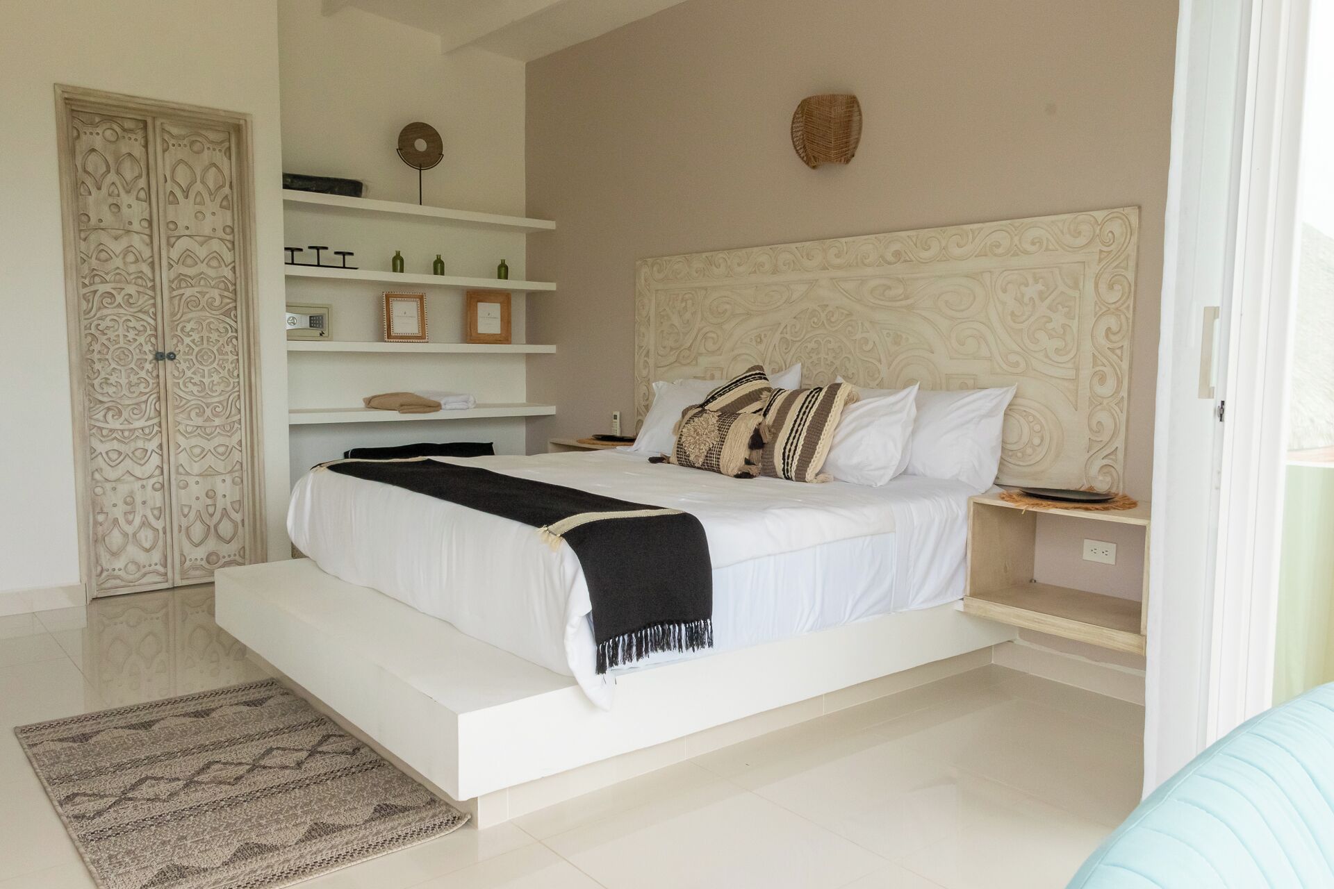 Quarto moderno com uma cama grande, mesa de cabeceira, guarda-roupa e prateleira com objetos decorativos.