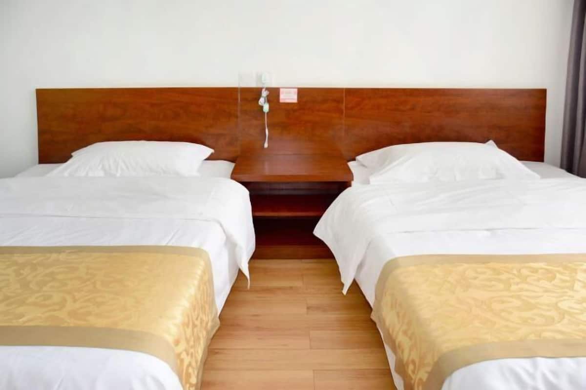 Quarto de hotel com duas camas de solteiro, cabeceira de madeira e uma pequena mesa no centro.