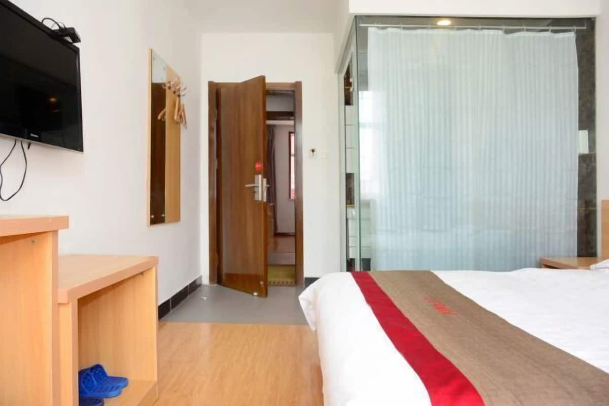 Quarto de hotel com cama, televisão fixada na parede, escrivaninha de madeira e porta que dá para um armário.