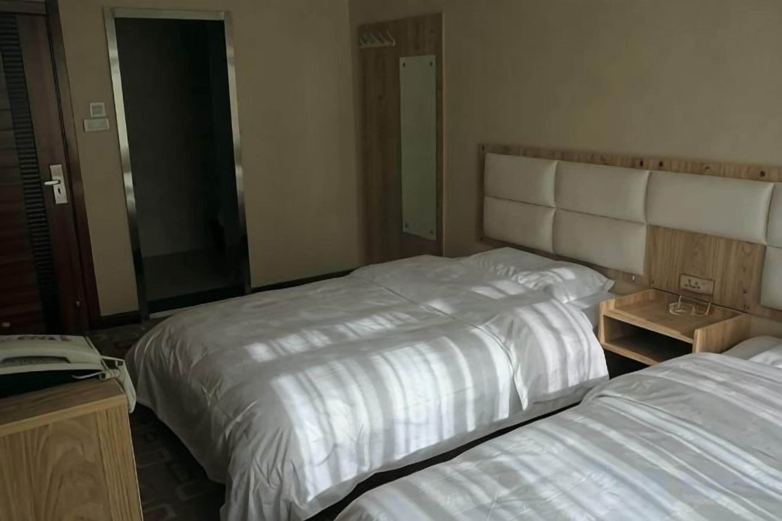 Quarto de hotel com duas camas, cabeceira de madeira, mesa de cabeceira e um espelho.