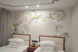 Quarto de hotel com duas camas, uma mesa de cabeceira com chaleira e parede decorativa com padrões de flores e folhas.