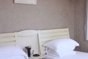 Quarto de hotel com duas camas, uma mesinha de cabeceira com telefone e um quadro na parede.