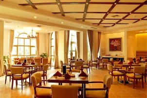 Uma sala de jantar ampla, com várias mesas e cadeiras, janelas grandes e um lustre.