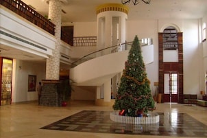 Um lobby com uma árvore de Natal central, uma escadaria e teto alto.