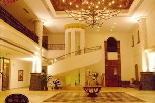 Um hall amplo com uma escadaria imponente, um candelabro e um balcão de recepção.
