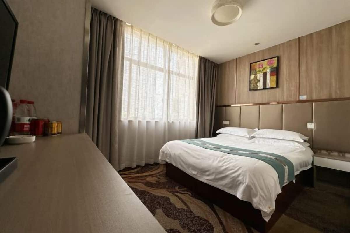 Quarto de hotel com cama, escrivaninha, televisão e janela com cortinas.