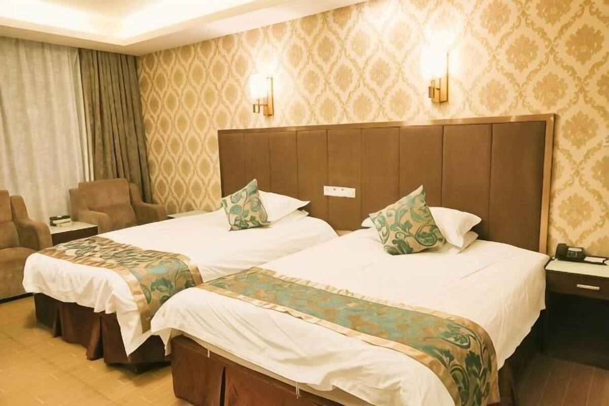 Quarto de hotel com duas camas, cabeceira, mesa de cabeceira, uma cadeira e parede estampada.
