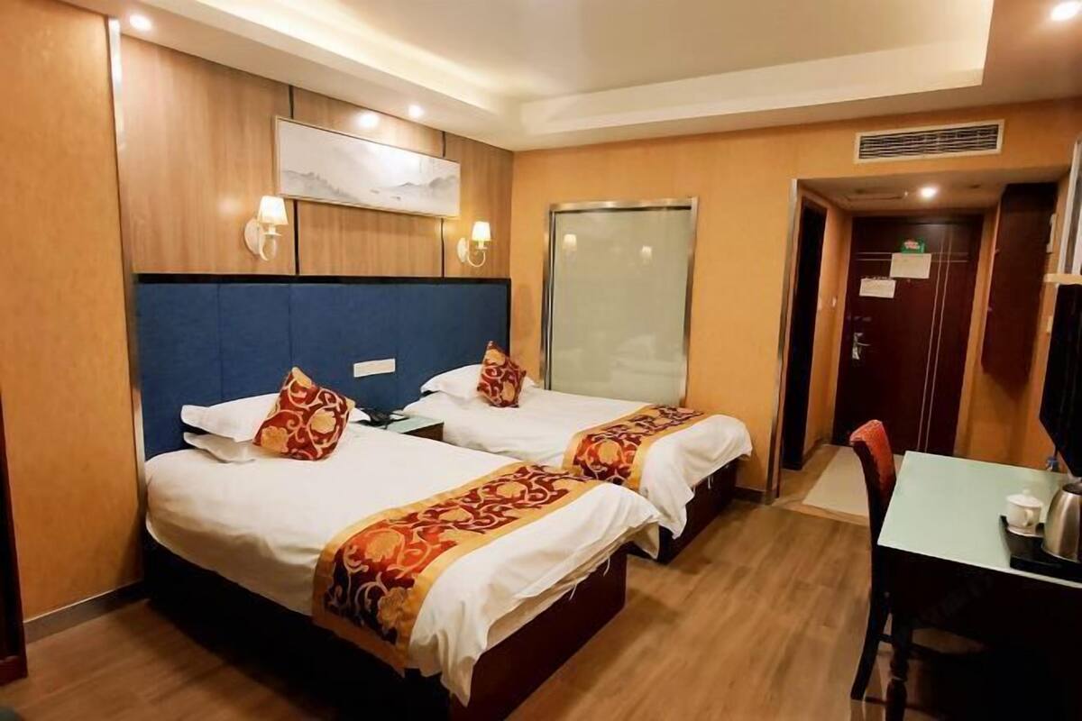 Quarto de hotel com duas camas, uma escrivaninha e uma cadeira.