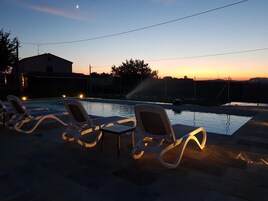 Piscina com espreguiçadeiras e pôr do sol ao fundo.