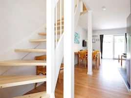 Um interior moderno com escada de madeira, área de jantar com cadeiras de madeira e uma TV de tela plana na parede.