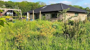 Uma casa com telhado inclinado, rodeada por um jardim exuberante com diversas plantas e flores.