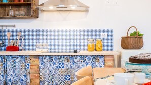 Cozinha com painel de azulejos, prateleiras de madeira e área de jantar com cadeiras e mesa.
