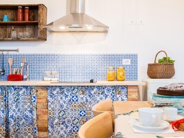 Cozinha com painel de azulejos, prateleiras de madeira e área de jantar com cadeiras e mesa.