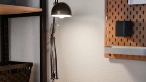 Uma luminária de mesa com acabamento metálico e cúpula preta, sobre uma superfície de madeira.