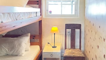 Quarto em dormitório com beliches, uma escrivaninha com luminária, uma cadeira e um radiador.
