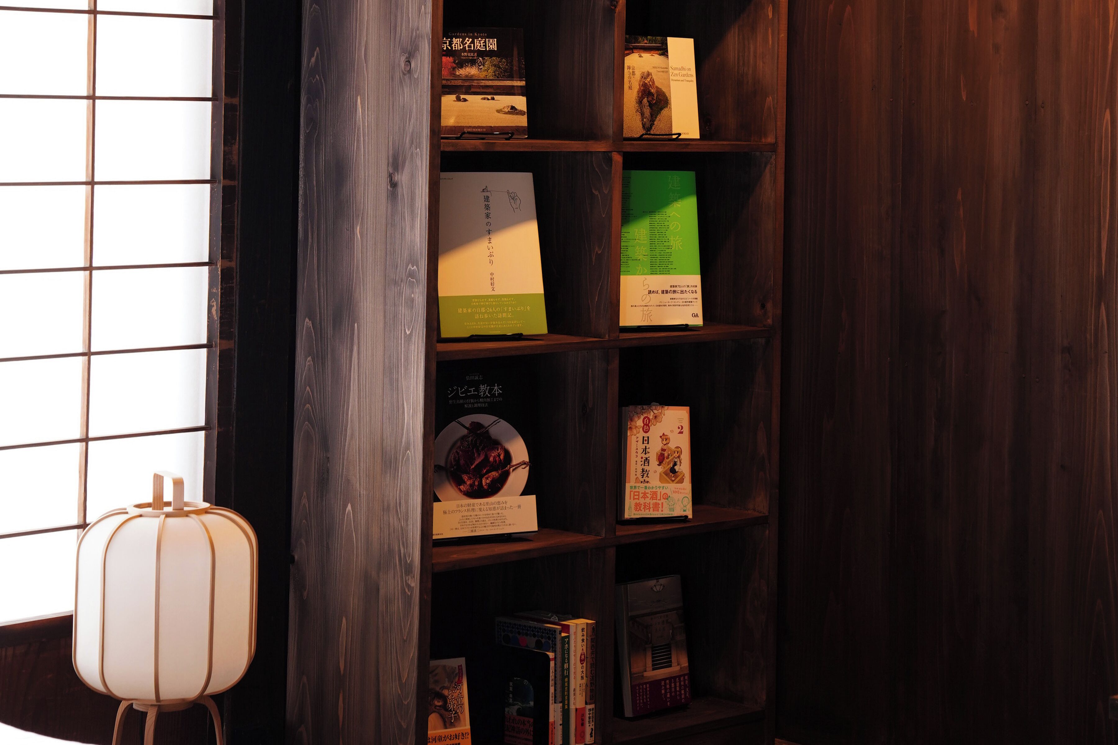 Uma estante com livros e uma luminária em um quarto com paredes de madeira e uma janela.