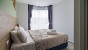 Quarto com cama, almofadas, mesa de cabeceira e janela com cortinas.