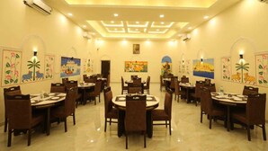 Uma área de refeições com várias mesas e cadeiras redondas, decorada com quadros e pinturas nas paredes.