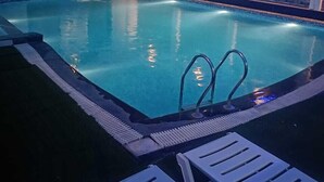Piscina com muro de pedra e nichos arqueados, rodeada por espreguiçadeiras.