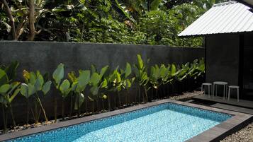 Piscina retangular com azulejos de mosaico azul, rodeada por um muro de pedra baixo e vegetação exuberante.