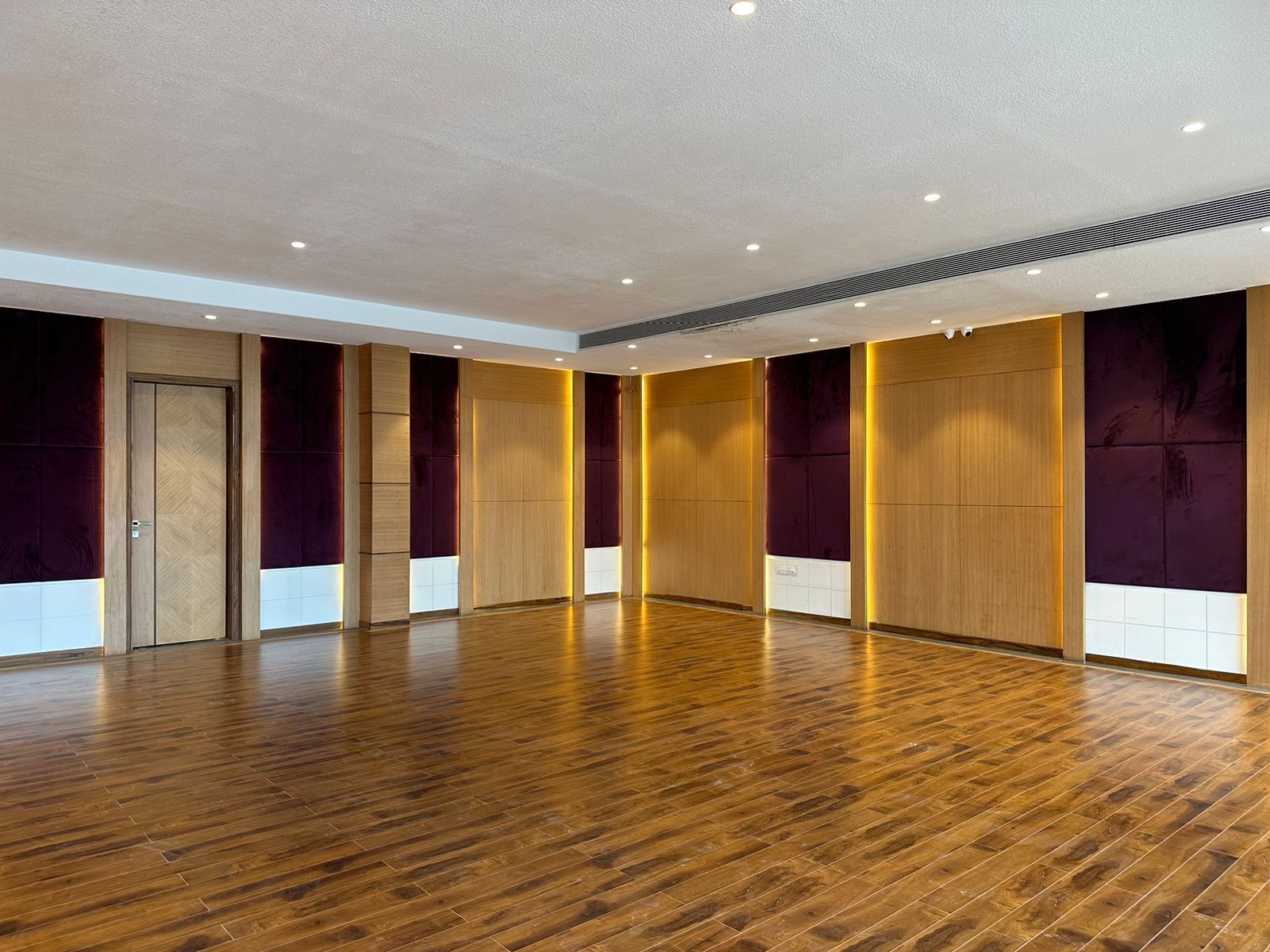 Quarto espaçoso com piso de madeira, uma porta e painéis de madeira verticais nas paredes, com listras verticais escuras.