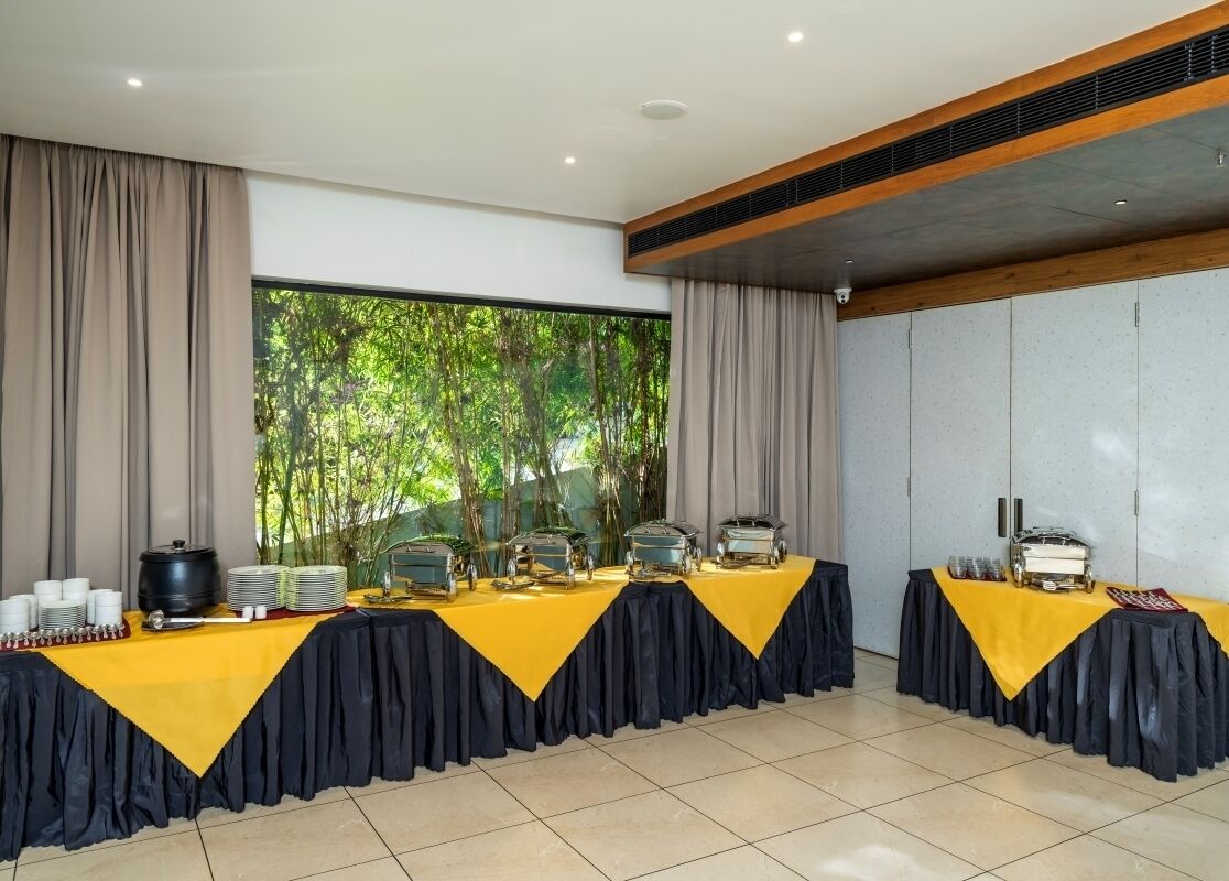 Uma sala de conferências com uma mesa comprida posta para um buffet, grandes janelas com vista para o verde e um design moderno no teto.