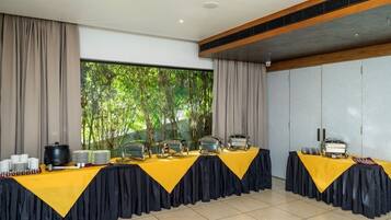 Uma sala de conferências com uma mesa comprida posta para um buffet, grandes janelas com vista para o verde e um design moderno no teto.