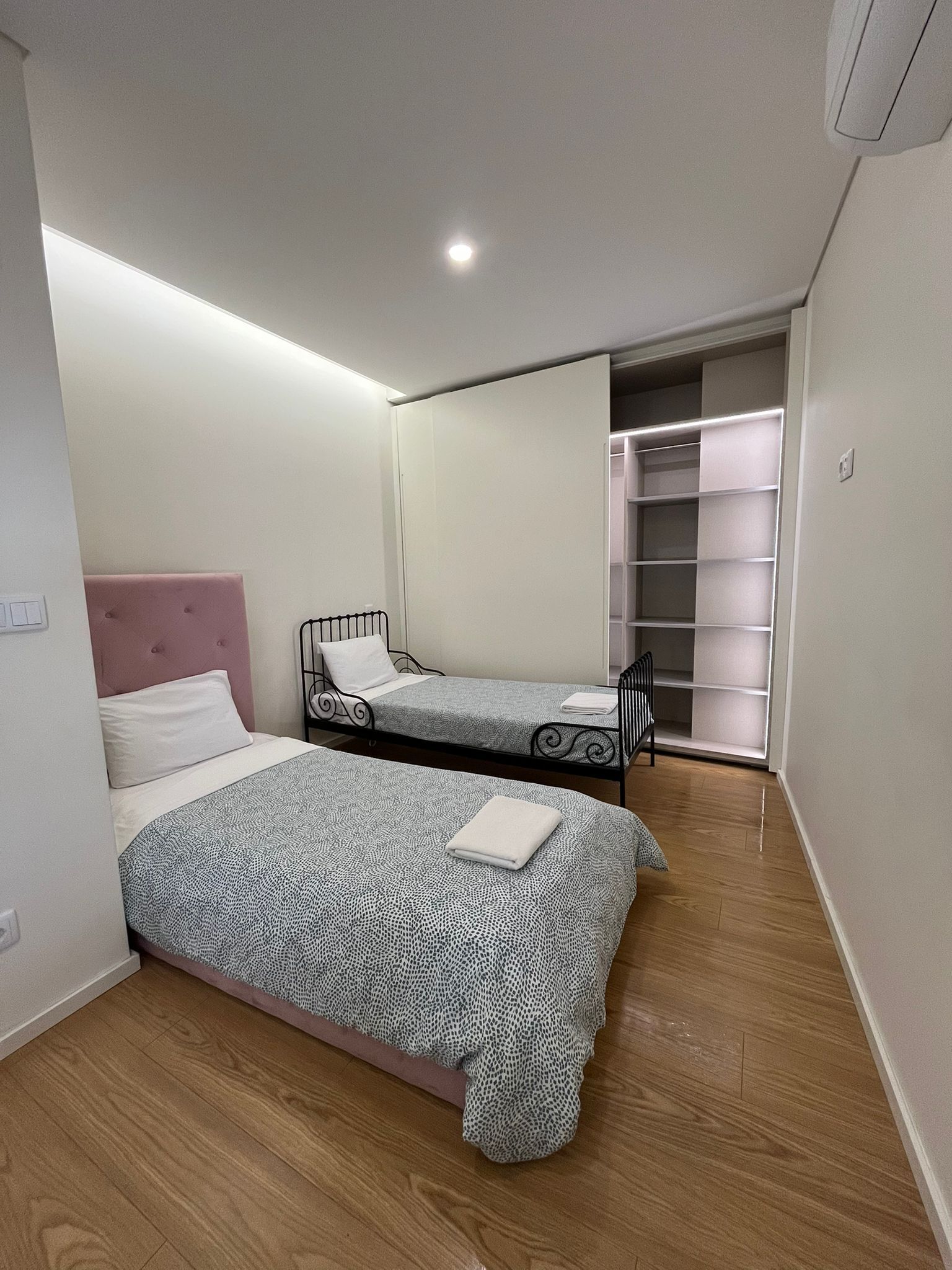 Quarto com duas camas, um guarda-roupa e um espelho.