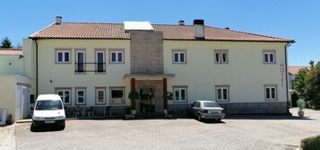 Um edifício de dois andares com telhado de telhas, entrada central e área de estacionamento com dois carros.