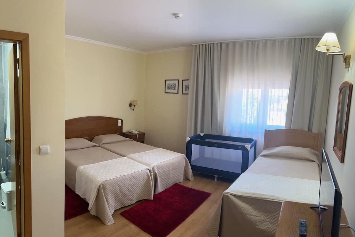 Quarto de hotel com duas camas, um tapete vermelho, uma escrivaninha com televisão e uma janela com cortinas.
