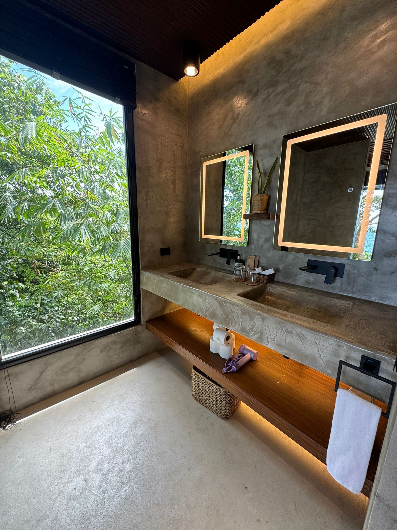 Casa de banho moderna com duas pias, um espelho grande e uma janela com vista para o verde.